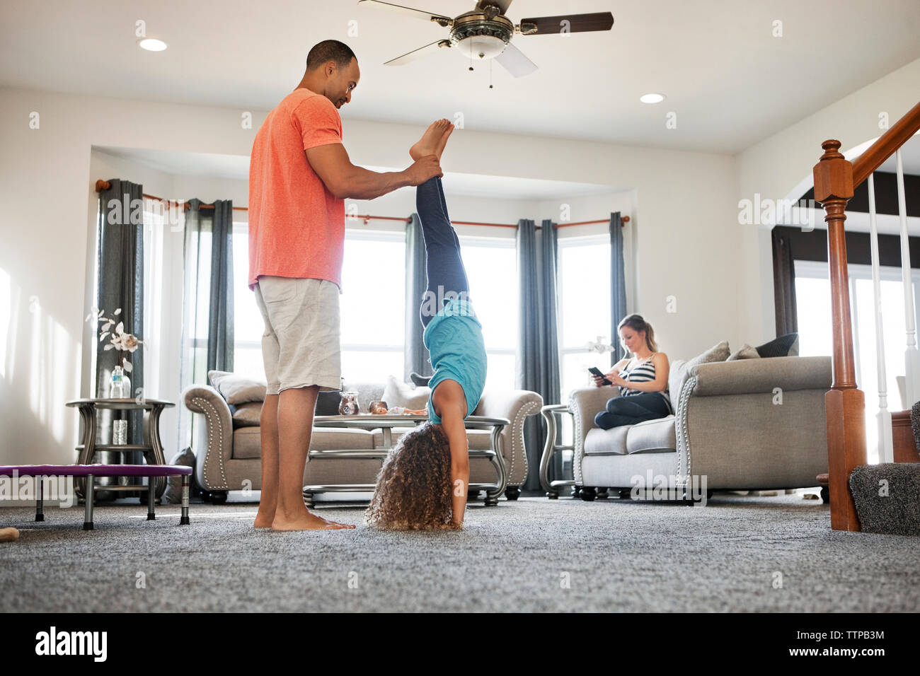 Father helping daughter doing handstand in living room at home Stock ...
