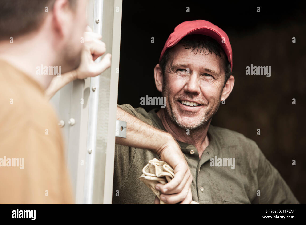 Happy farm worker looking at friend while standing at barn Stock Photo ...