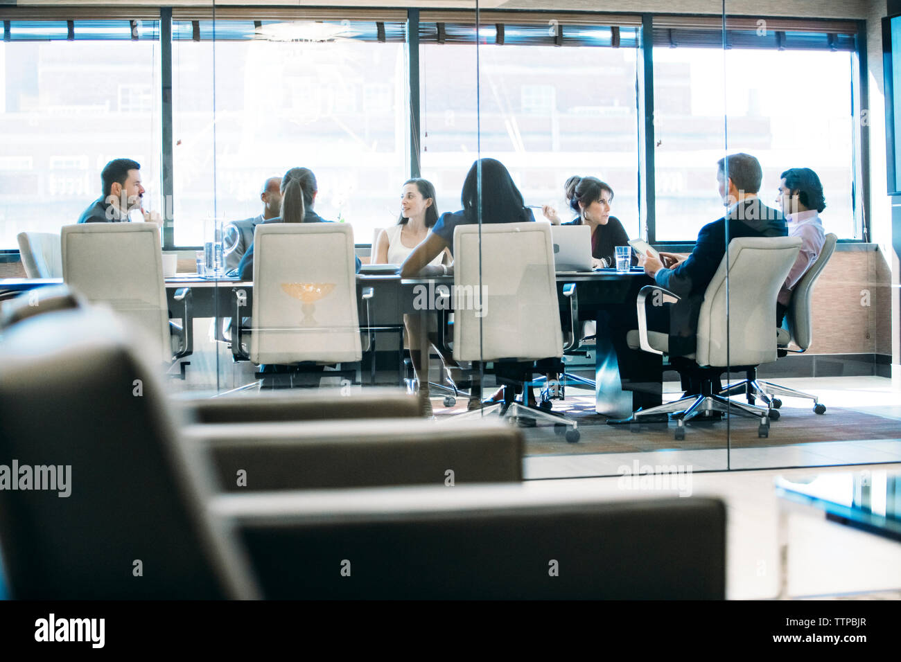 business people discussing in meeting at board room seen through window ...