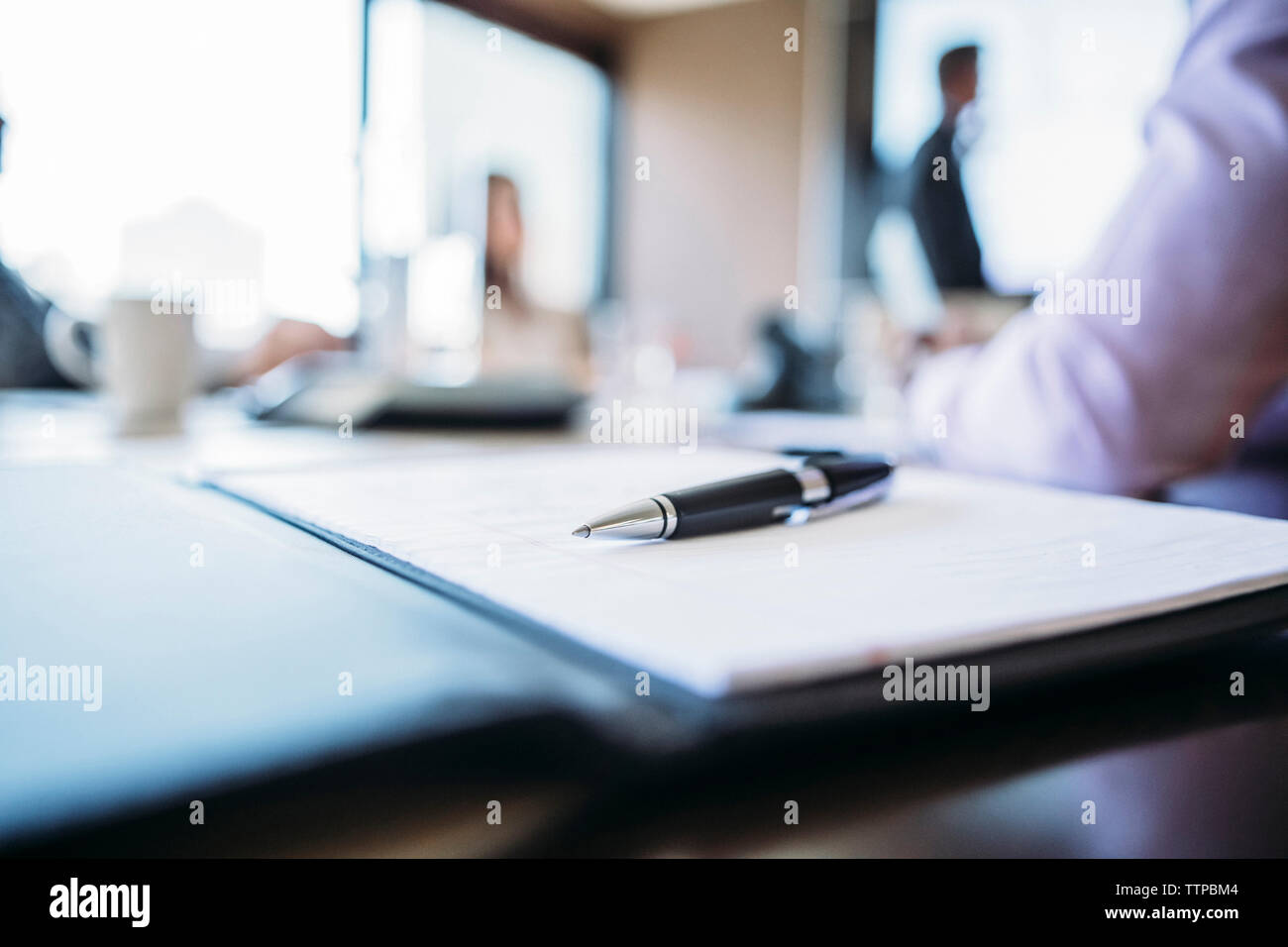 Close-up of pen and document on table with business people in ...