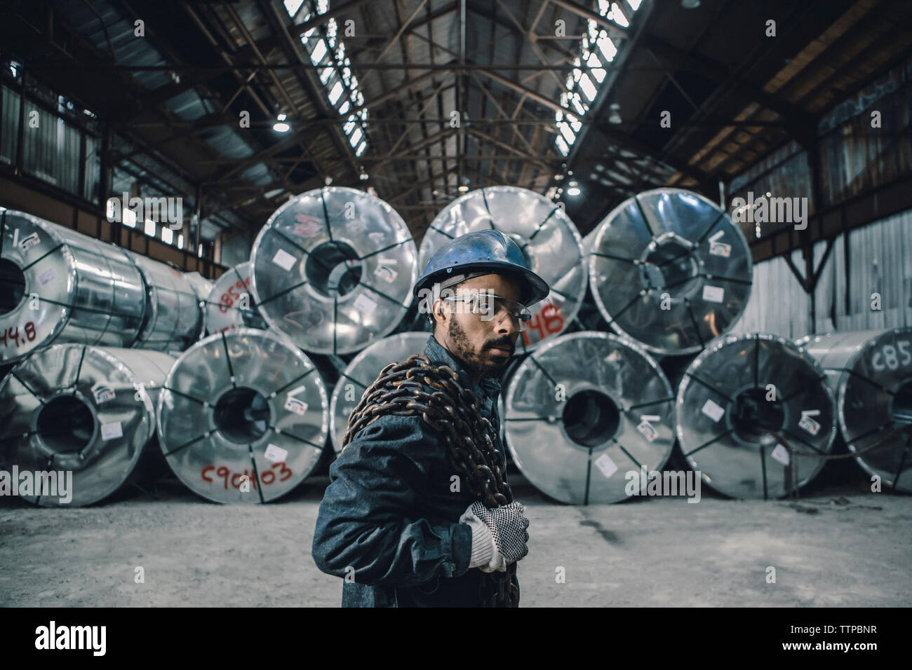 Portrait of male worker carrying chain while standing against rolled up ...