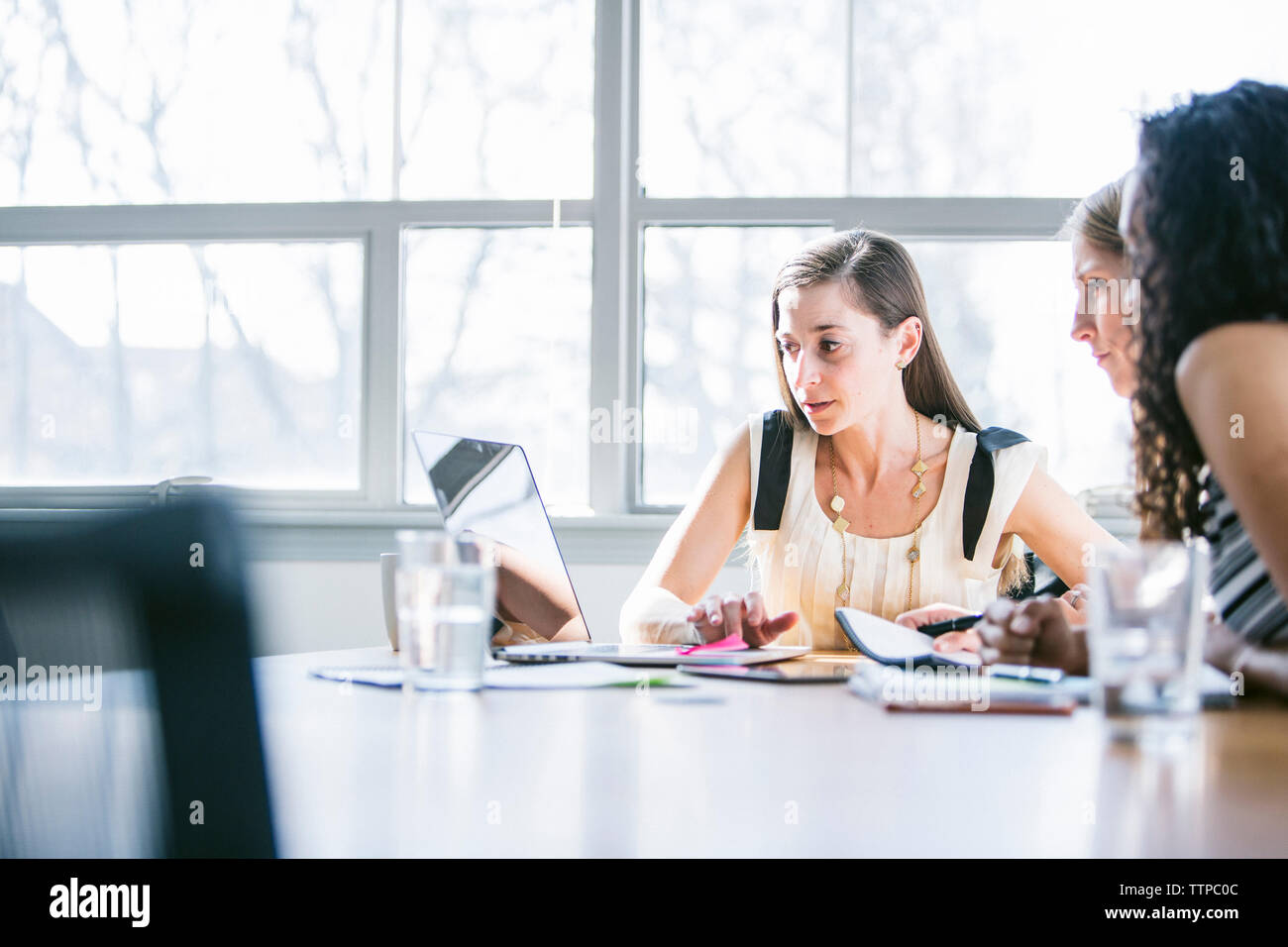 Female colleagues looking at laptop computer while working in board ...