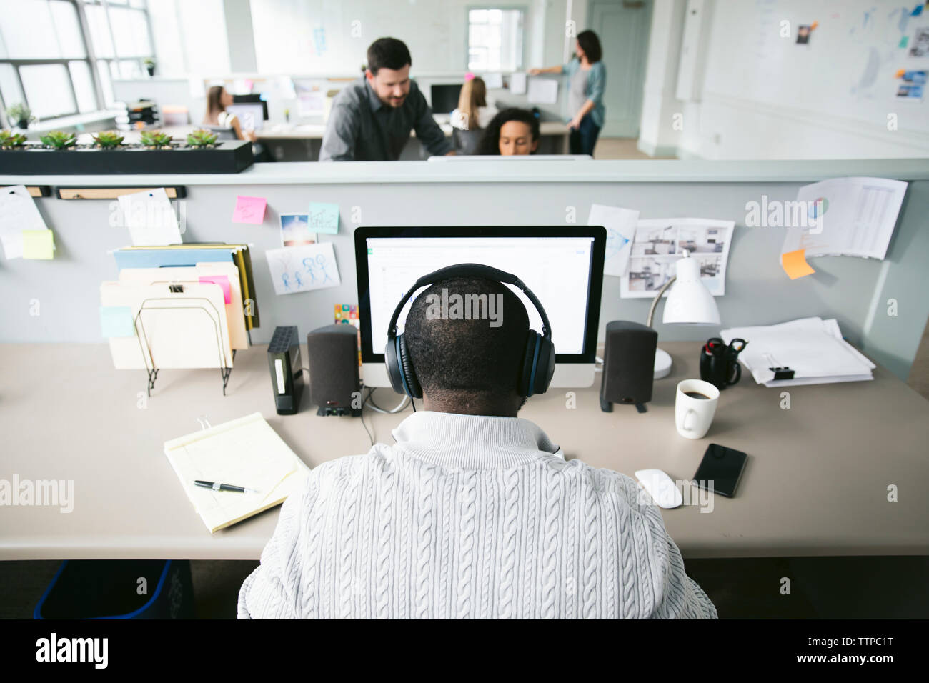 Rear view of businessman working on desktop computer with colleagues in ...