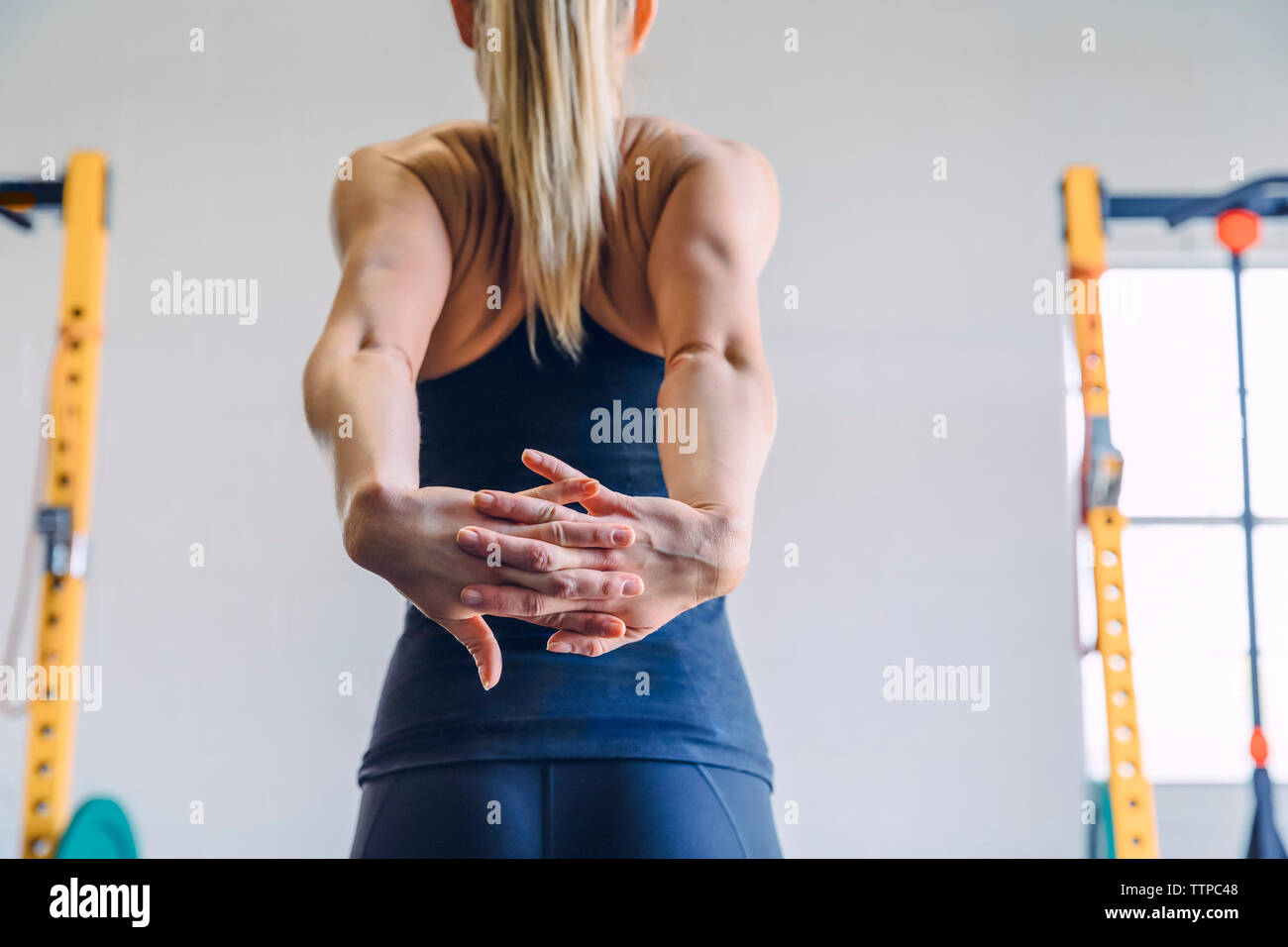 Rear view of woman stretching hands behind back while exercising in gym ...