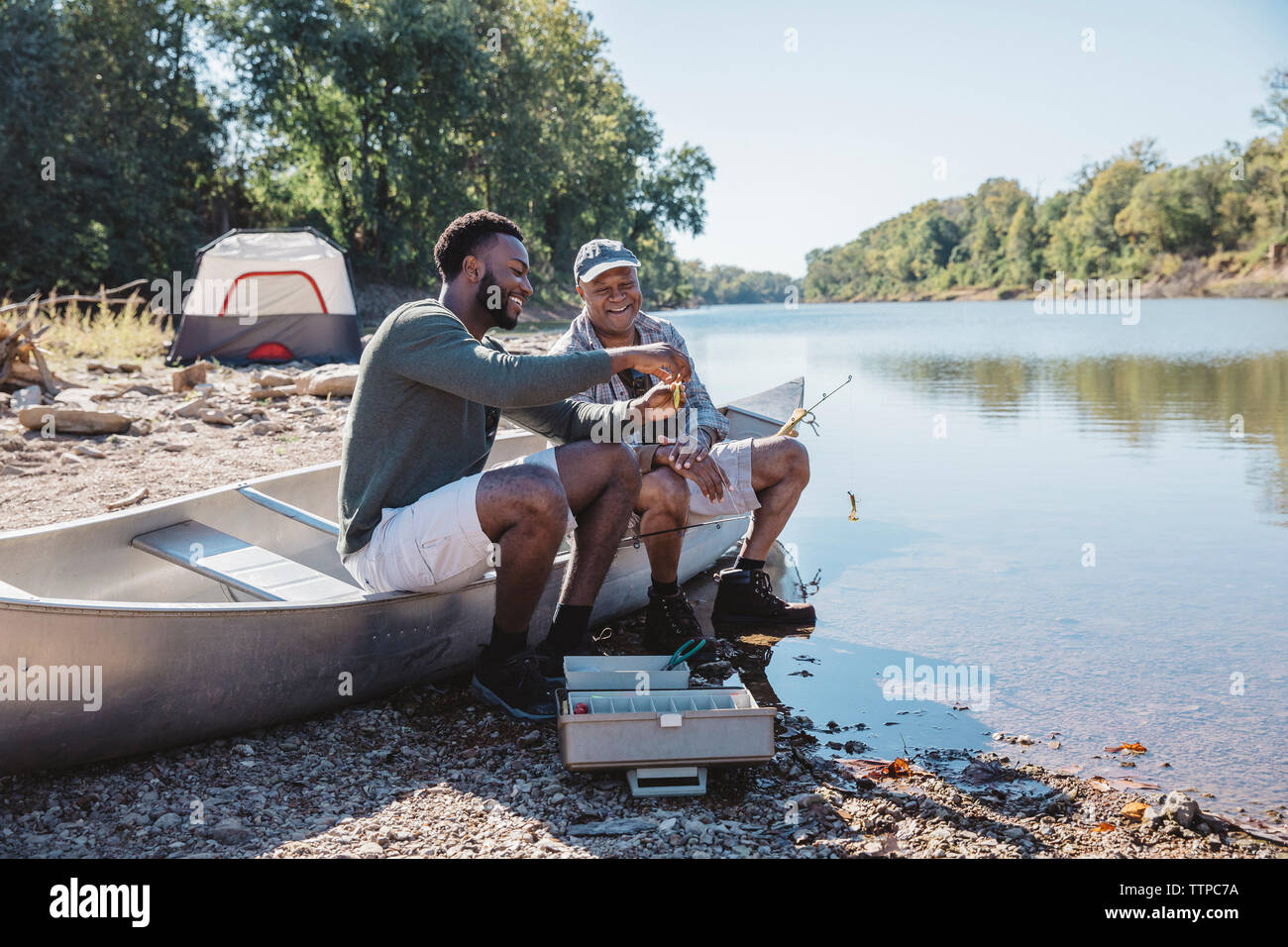 Happy male friends adjusting fishing tackle on boat at lakeshore Stock ...