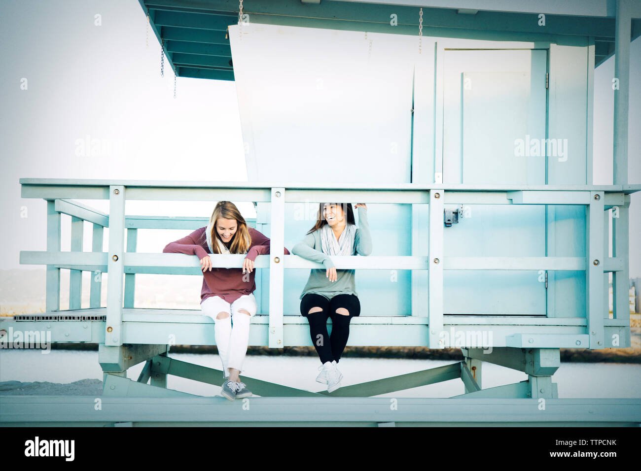 Happy female friends sitting on lifeguard hut at beach Stock Photo - Alamy