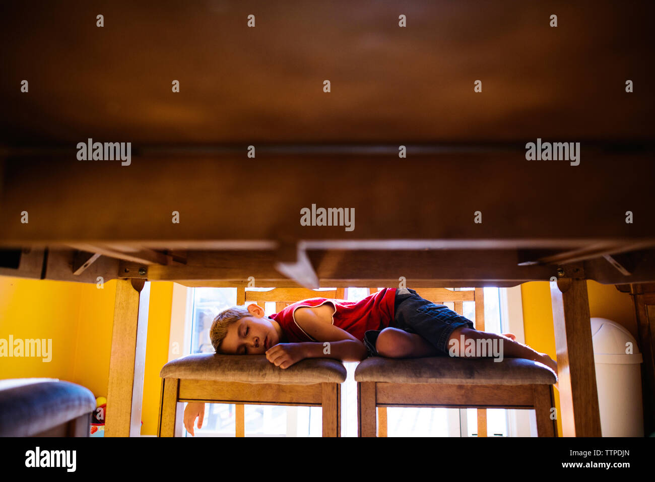 Boy sleeping on chairs at home seen from underneath table Stock Photo ...