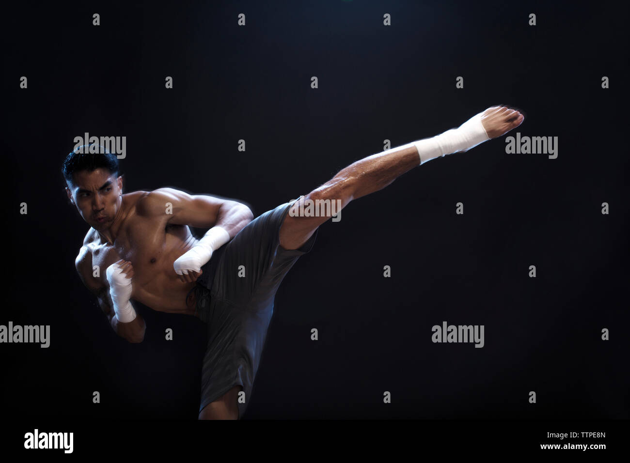 Determined male kickboxer kicking against black background Stock Photo ...