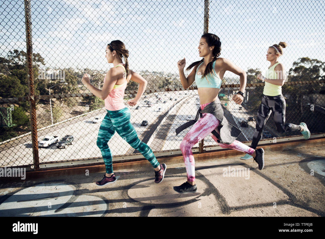 Side view of sporty women jogging by fence on bridge Stock Photo - Alamy