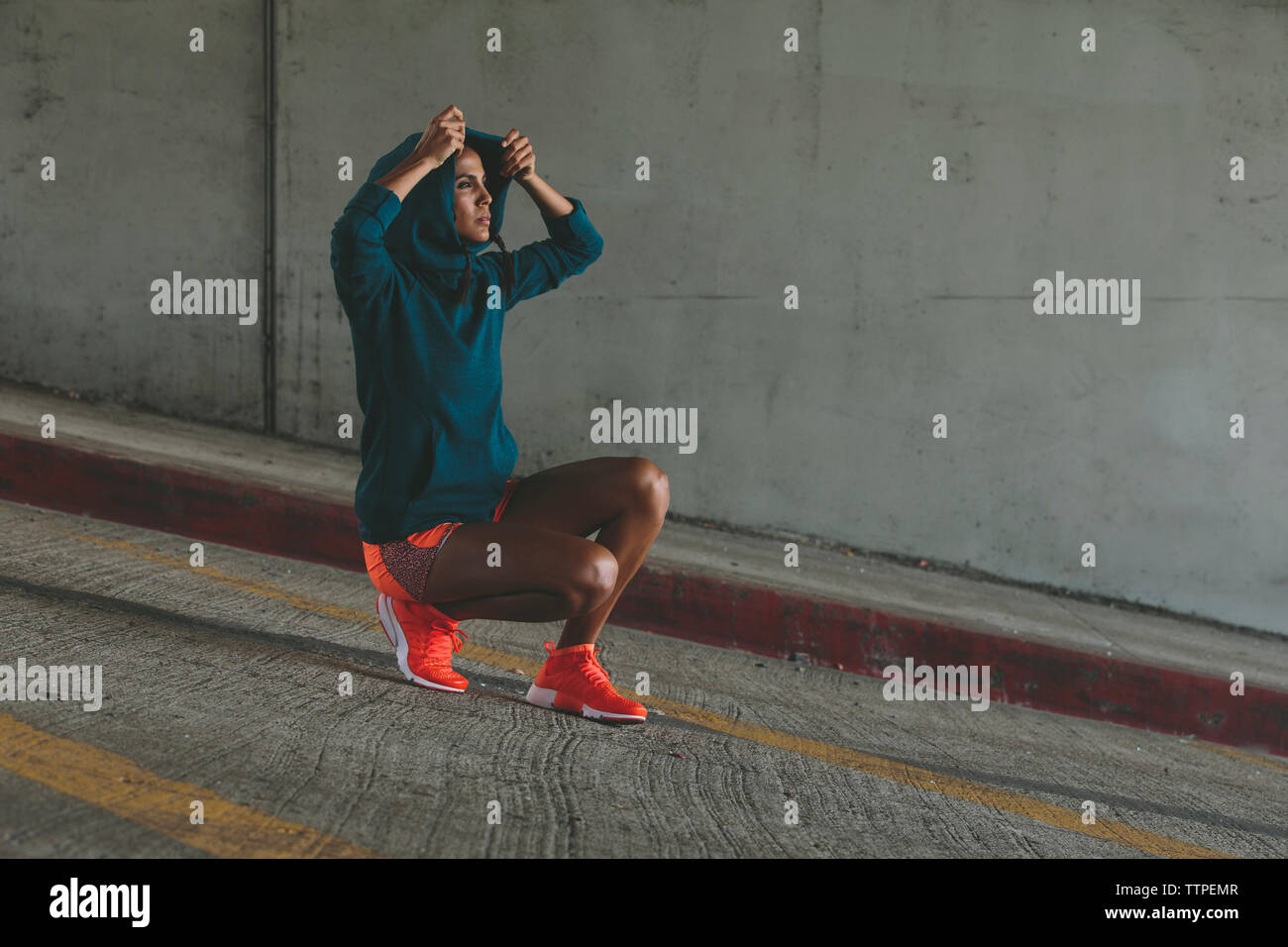Woman putting on hood while crouching at road Stock Photo - Alamy