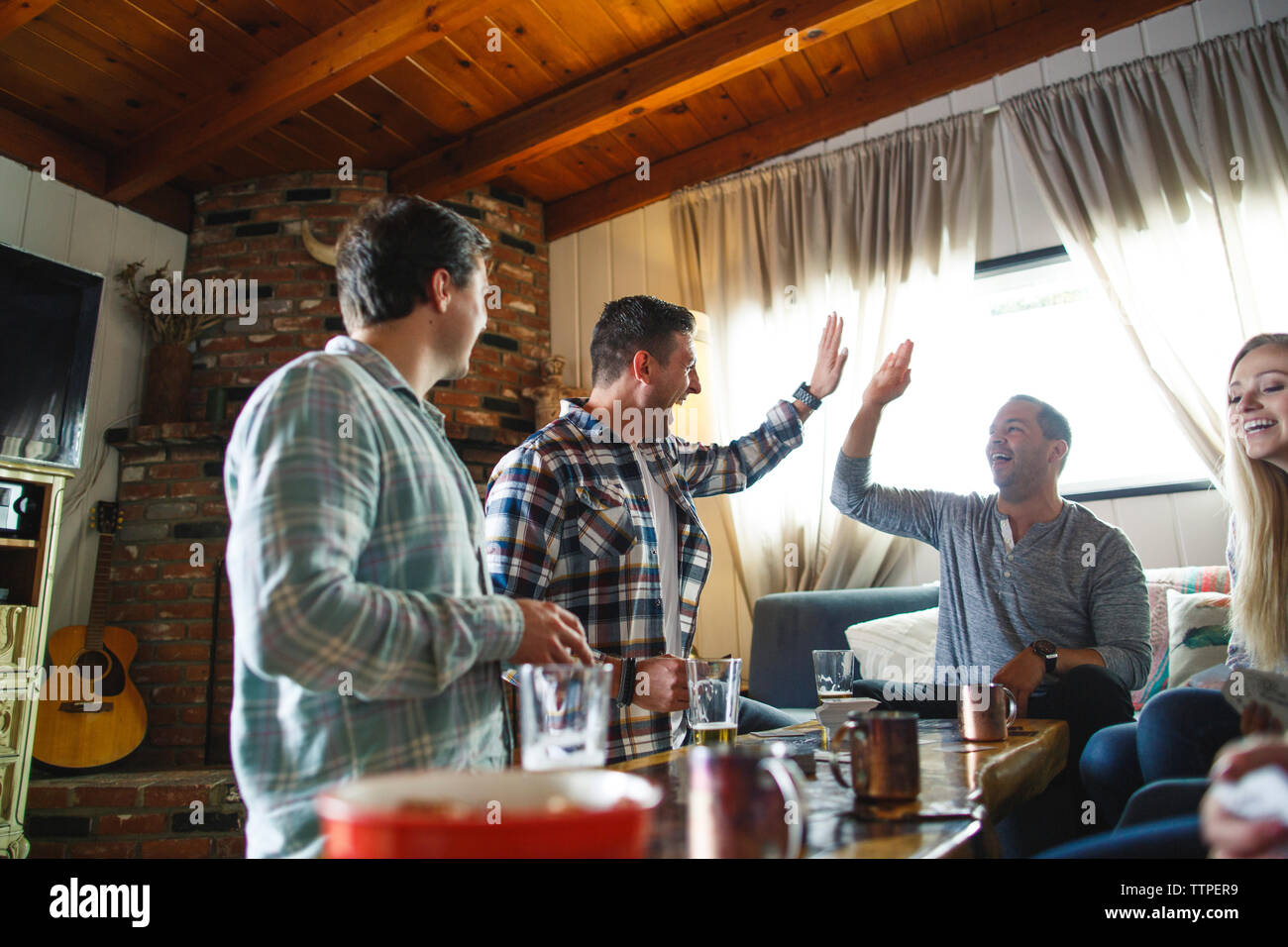 Happy friends giving high-five while playing card game at home Stock ...