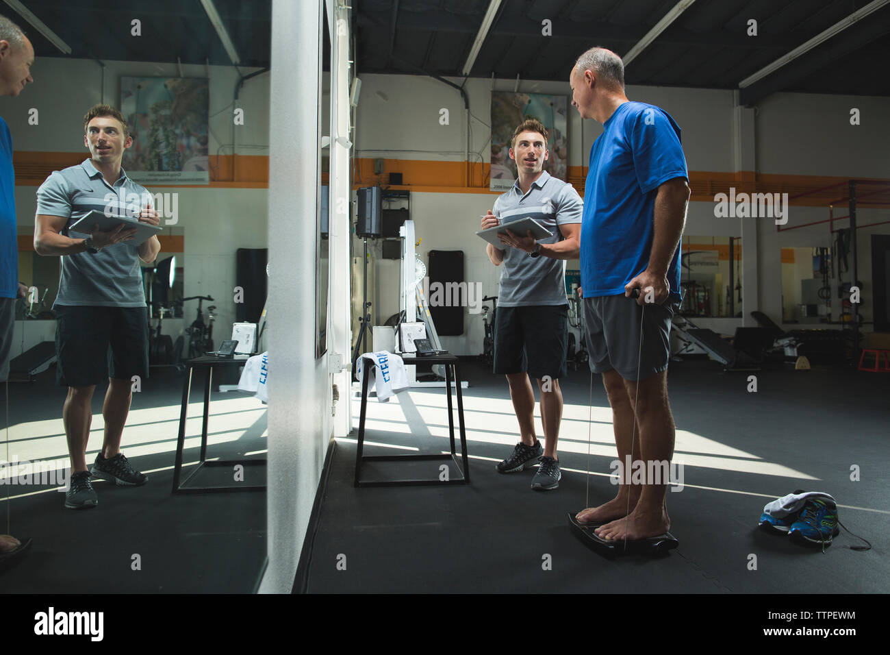 Trainer with tablet computer talking with man practicing stretching in ...