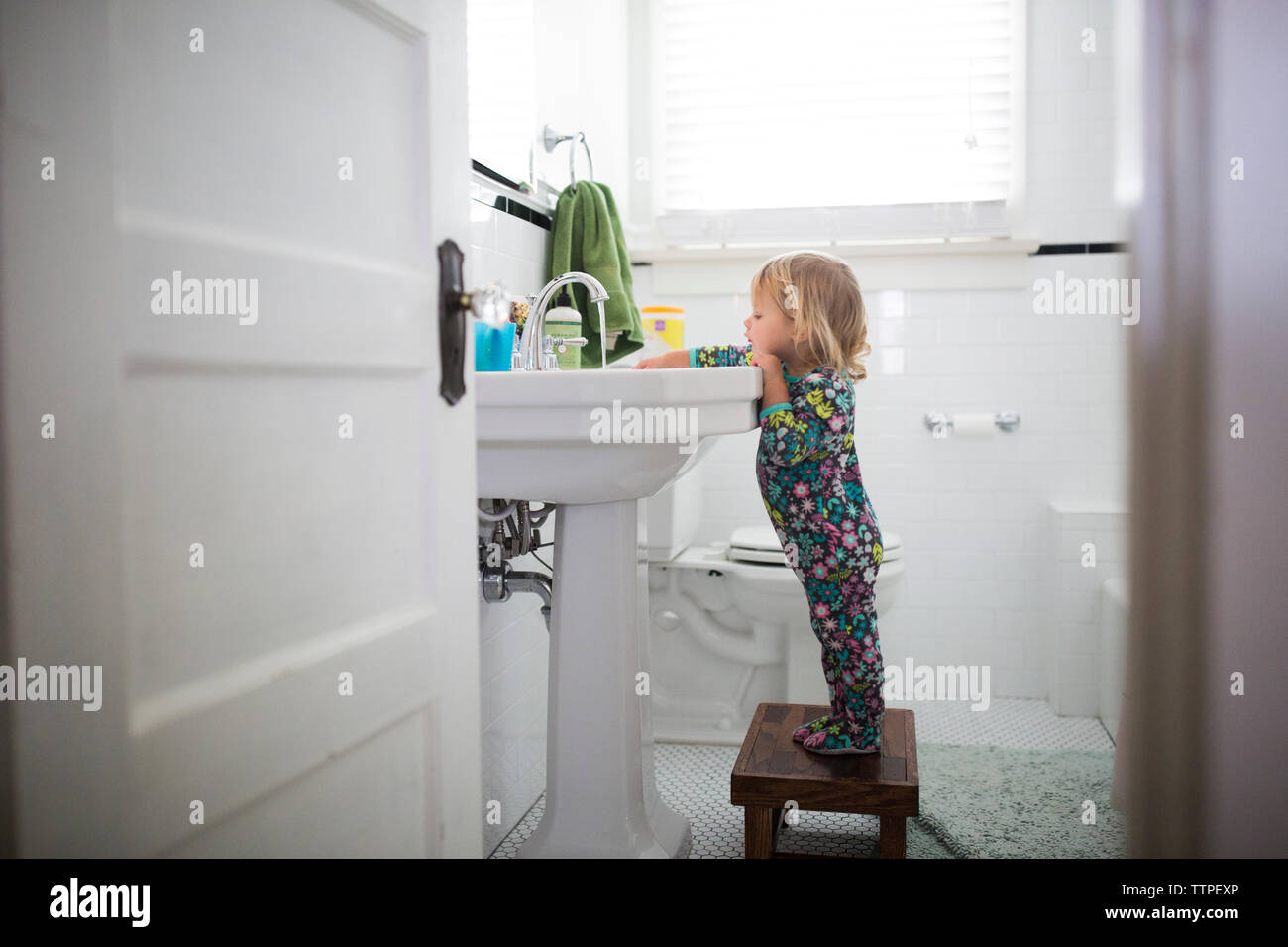 Side view of baby girl standing on stool by bathroom sink Stock Photo ...