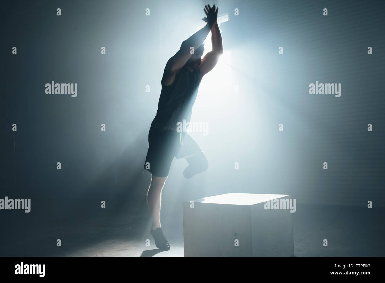 Adaptive athlete with arms raised jumping on box in gym Stock Photo - Alamy