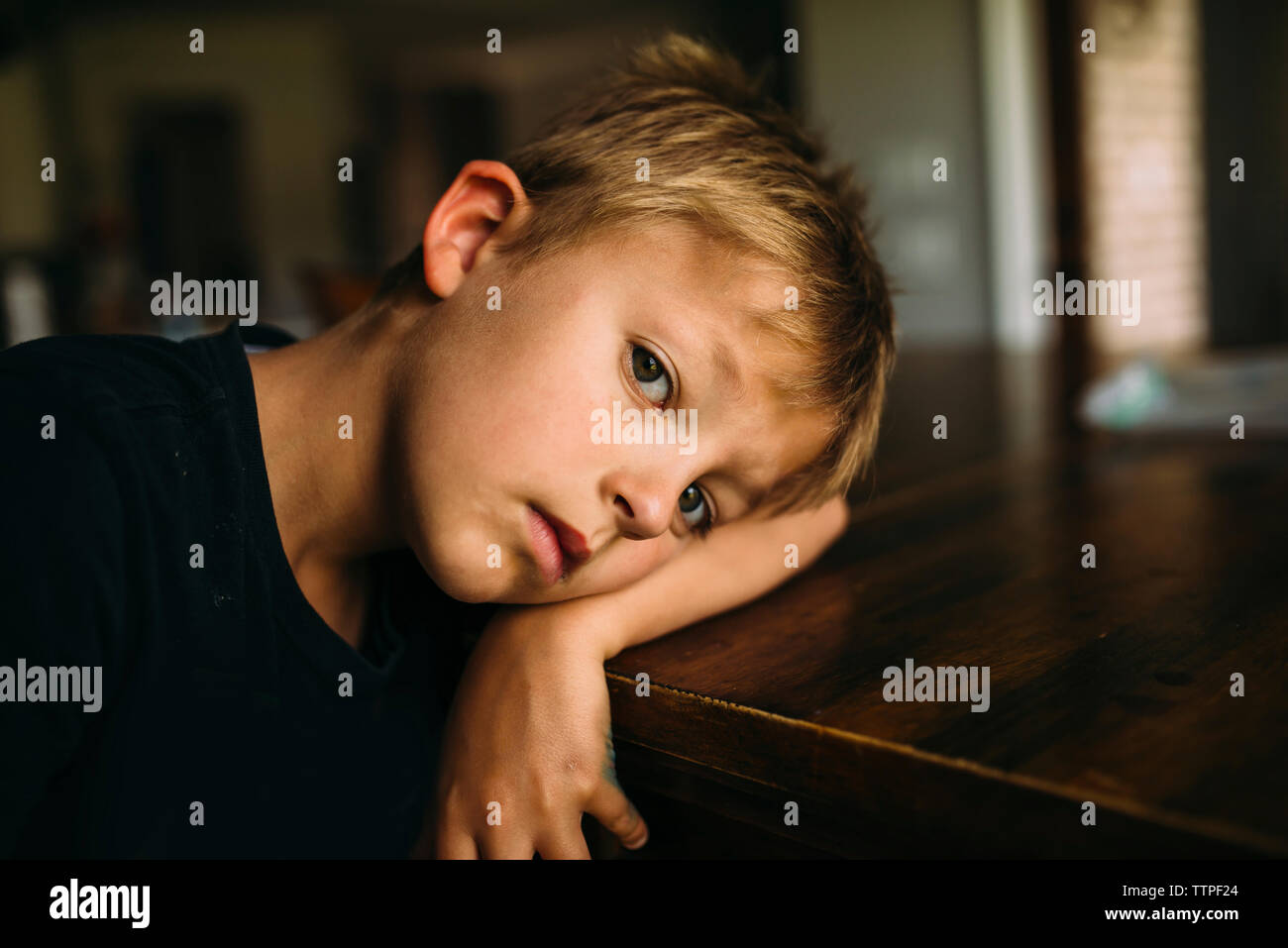 Portrait of serious boy lying head on table at home Stock Photo - Alamy