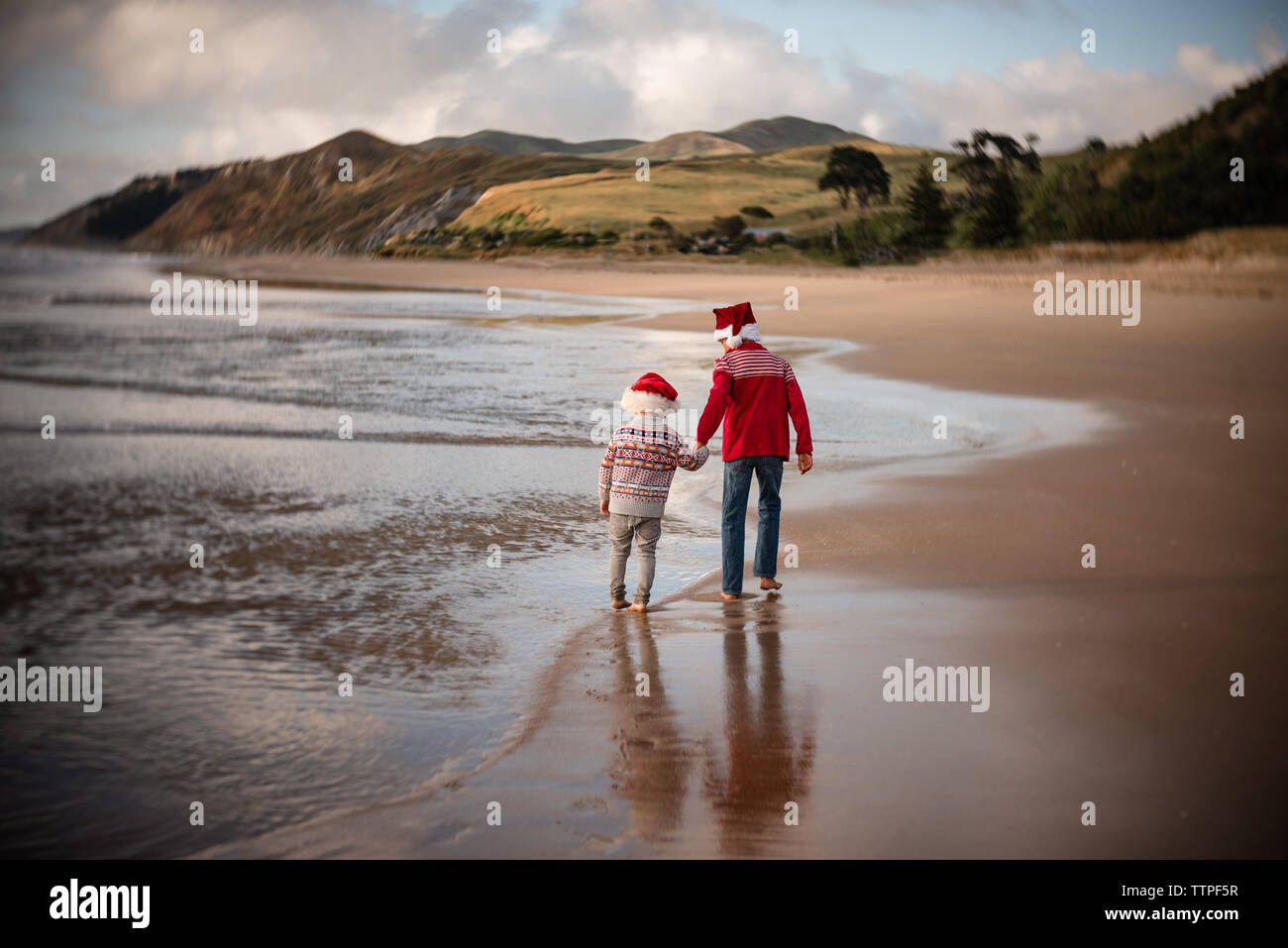 Two boys wearing Santa hats walking on a beach with mountains Stock ...