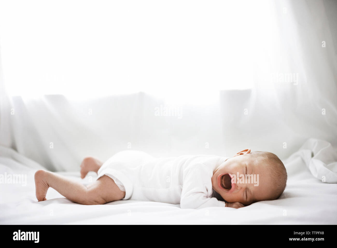 Side view of baby girl crying while lying on bed at home Stock Photo ...