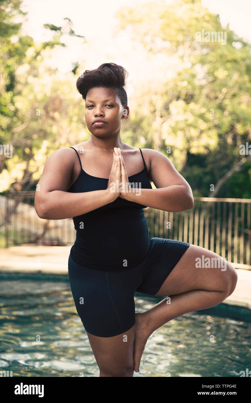 Portrait of confident young woman doing tree pose at poolside Stock ...