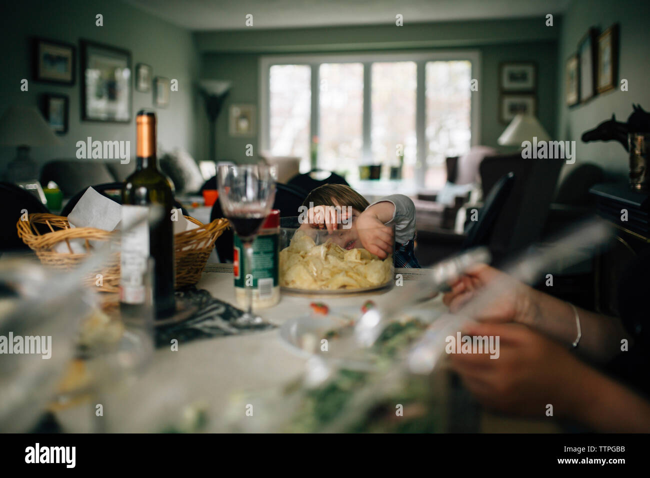 Boy taking potato chips from bowl at dining table Stock Photo - Alamy