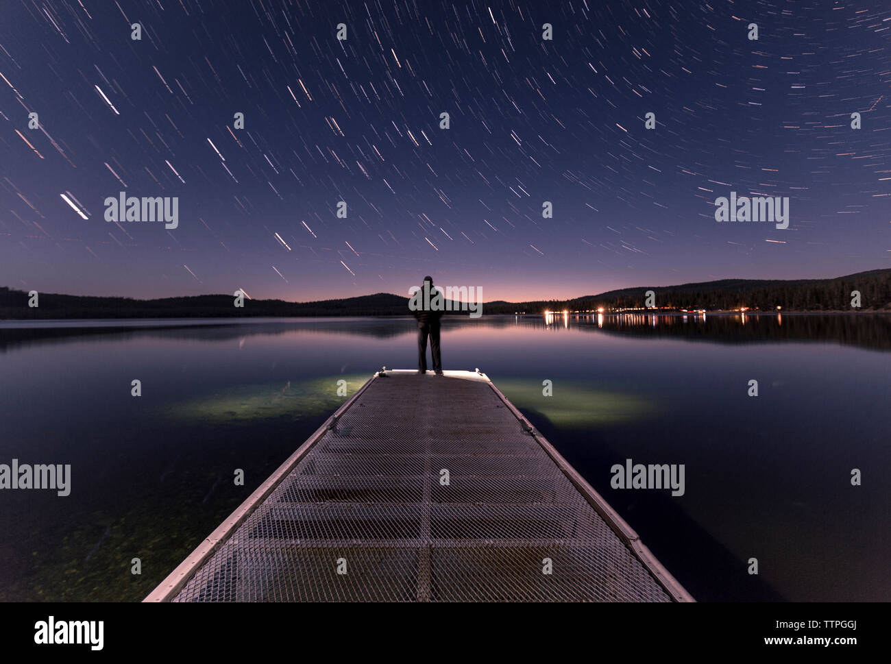 Man standing on jetty and looking at star trail Stock Photo - Alamy
