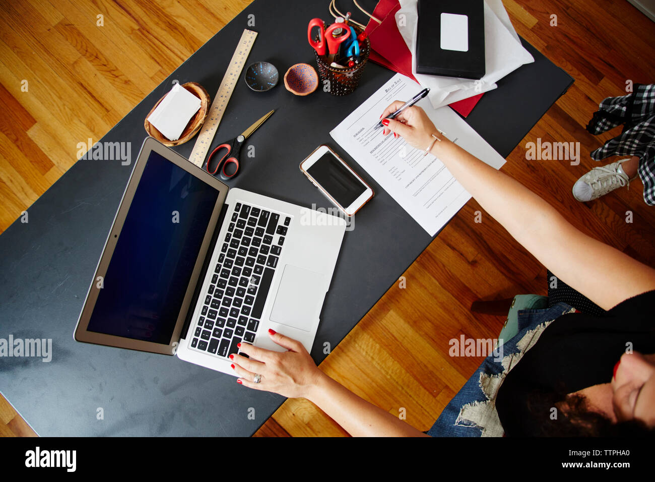 Overhead view of owner using laptop while writing on paper at table in ...