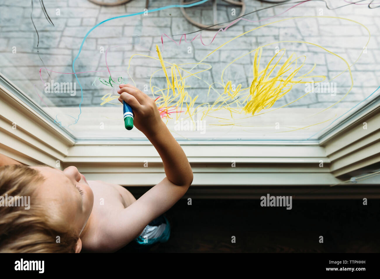 Overhead view of shirtless boy writing on window at home Stock Photo ...