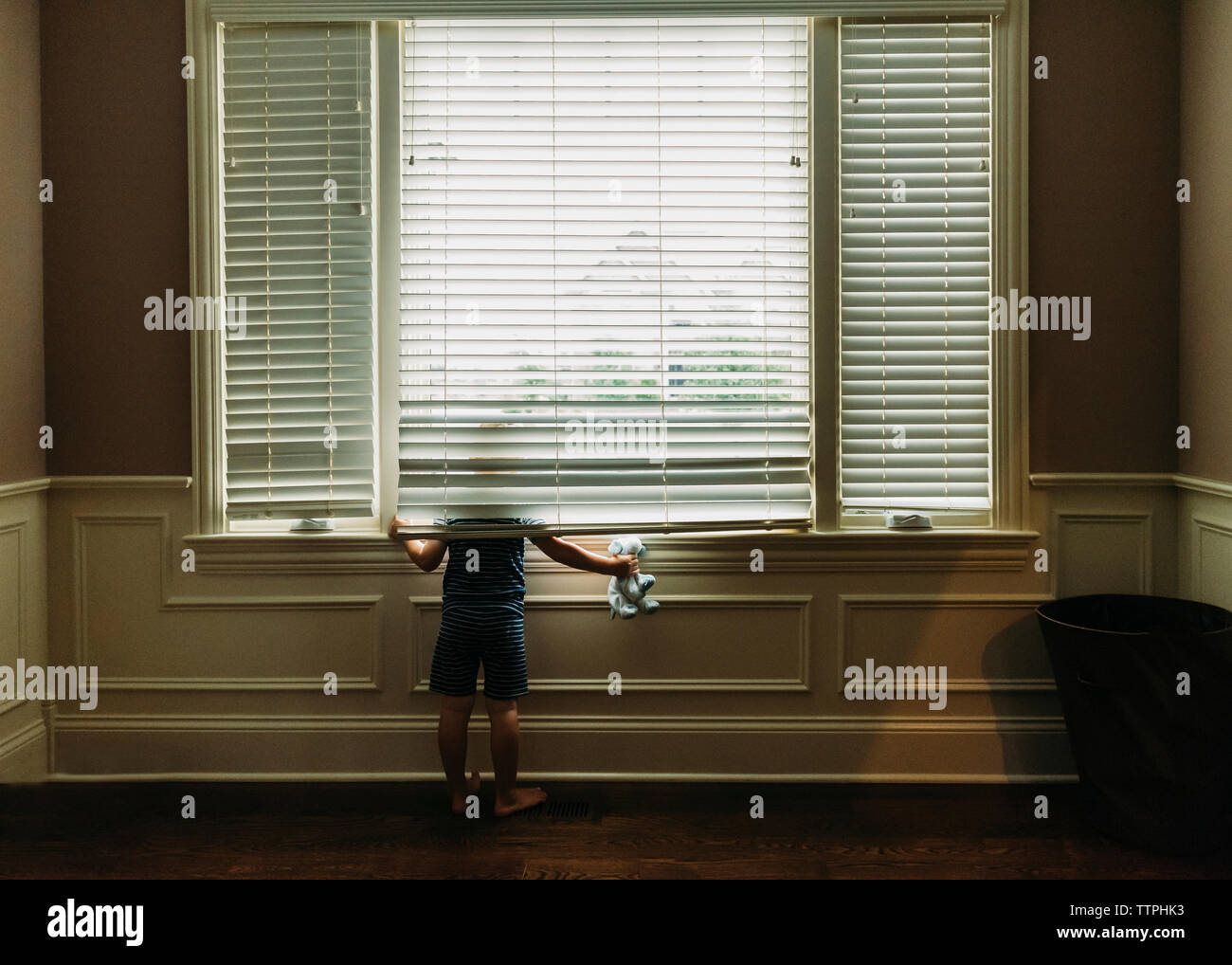 Rear view of boy with toy looking through window Stock Photo - Alamy