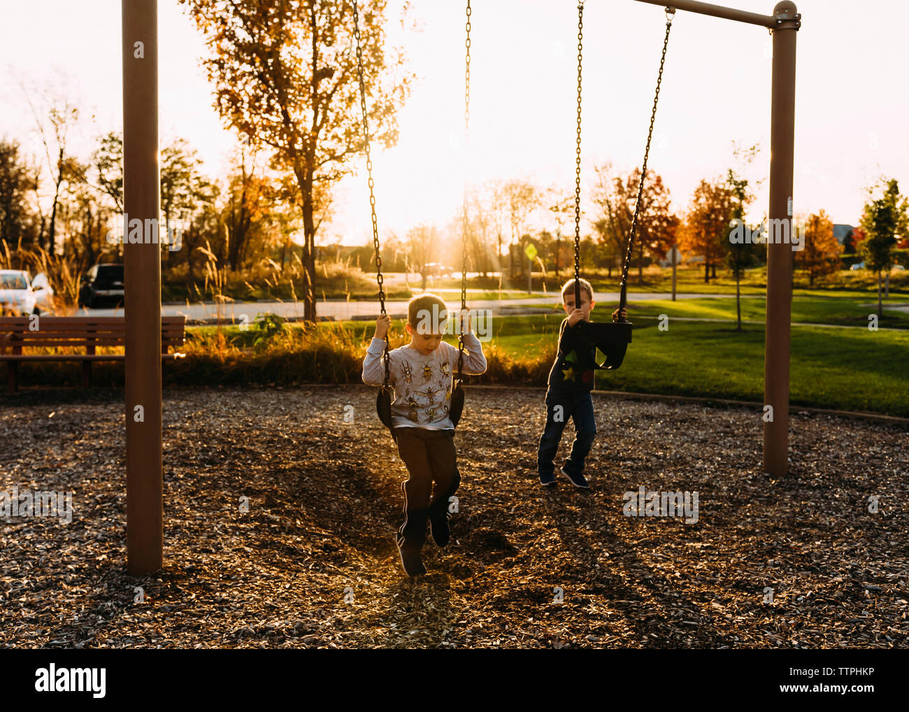 Brothers playing on swing in playground against clear sky Stock Photo ...