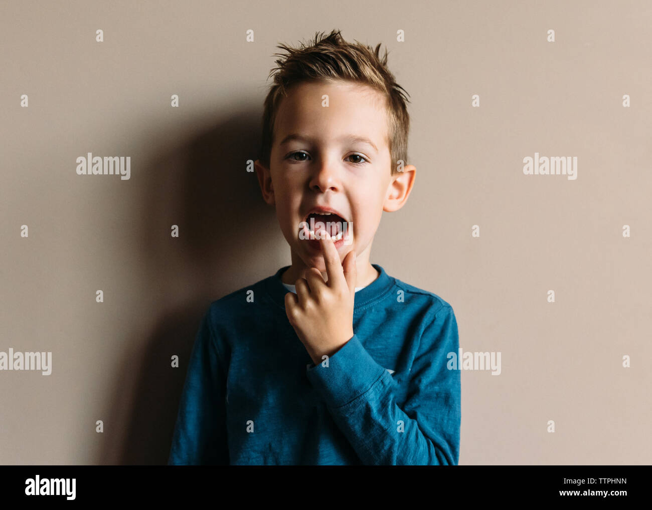 Portrait of boy touching teeth while standing against wall at home ...