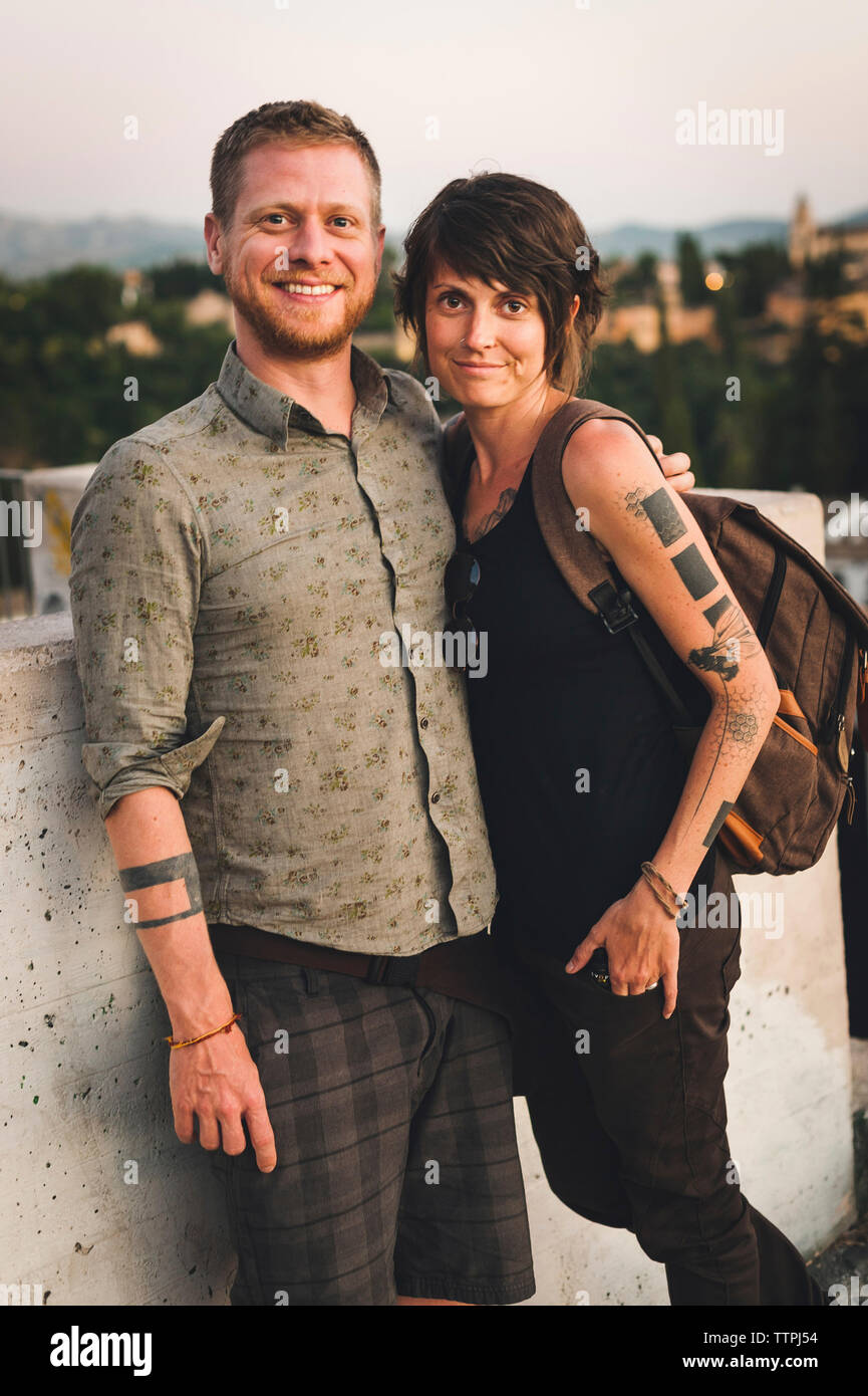 Portrait Of Confident Tattooed Couple Standing Against Retaining Wall