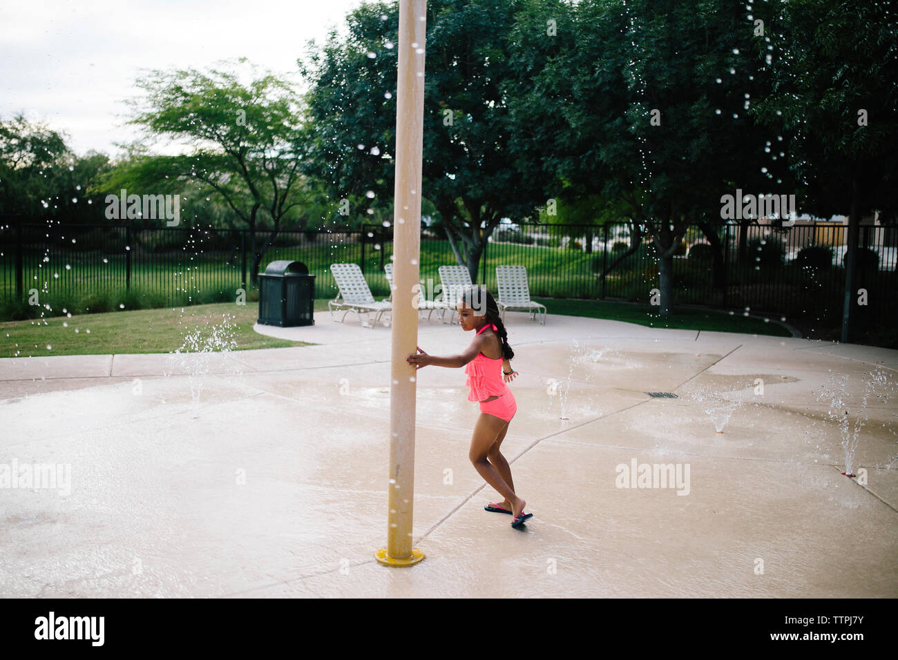 Side view of girl wearing swimwear playing with fountain in water park ...