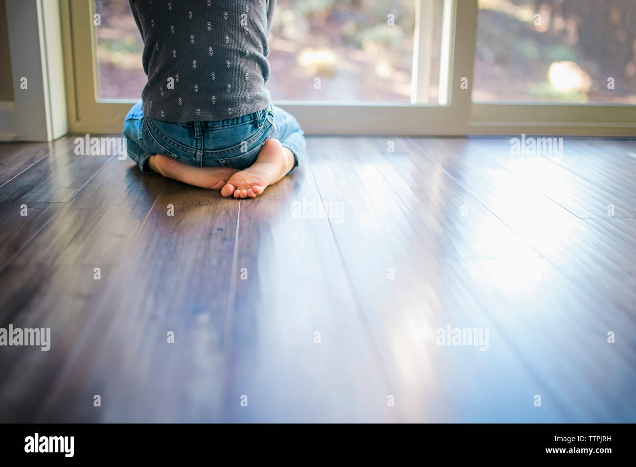 Low section of girl kneeling on hardwood floor by window at home Stock ...