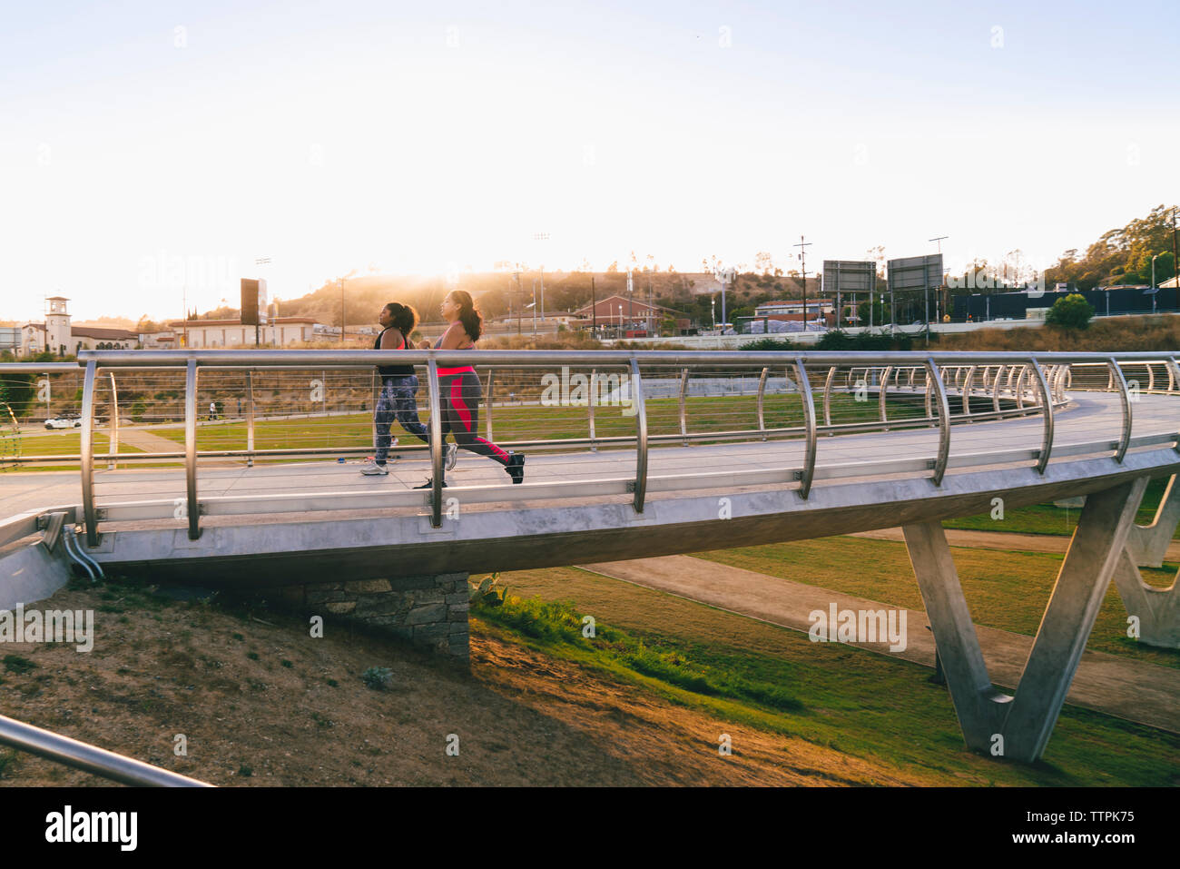 Side view of female friends jogging on elevated walkway against clear ...