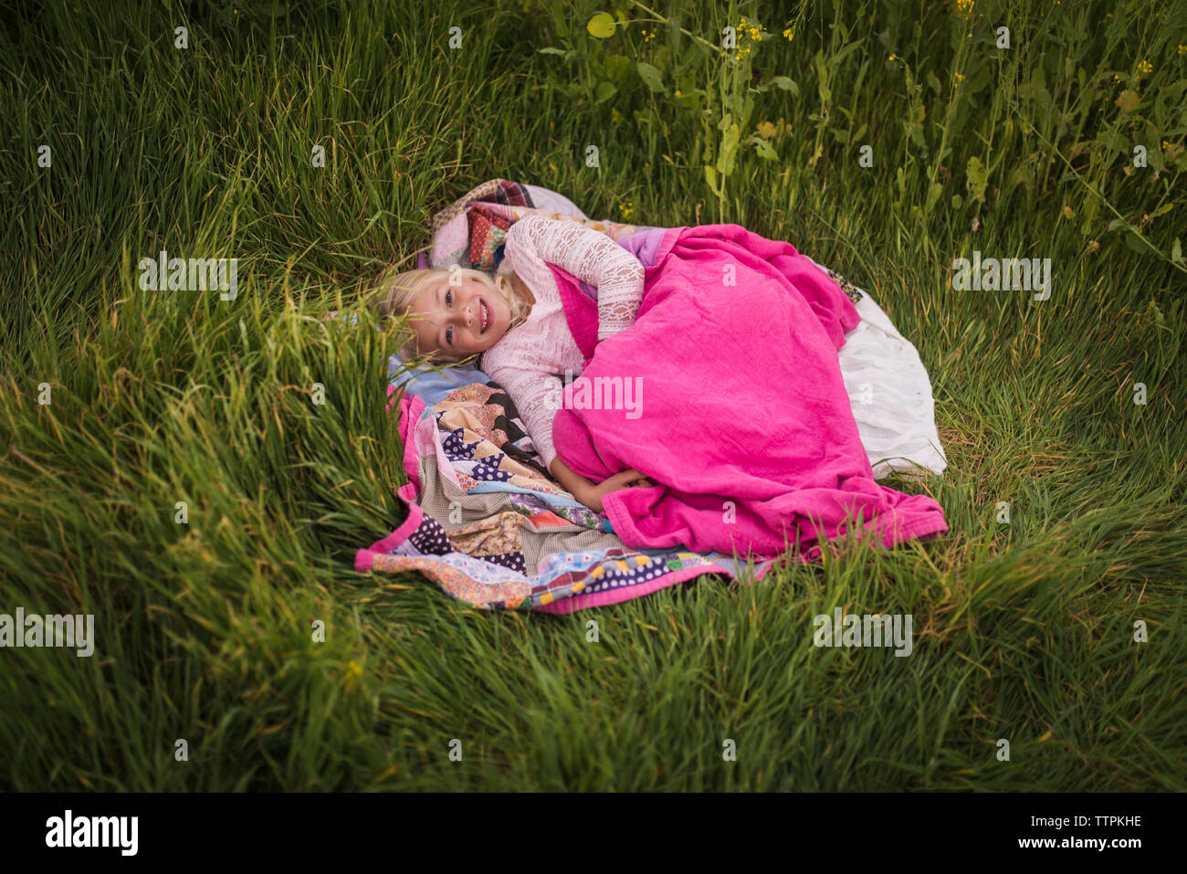 High angle portrait of happy girl lying on blanket amidst grassy field ...