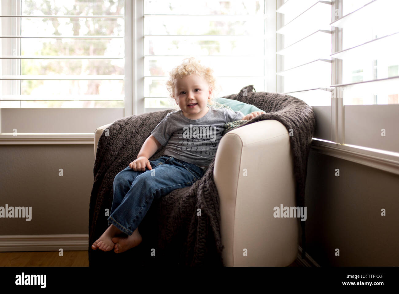 Portrait of cute boy sitting on chair against windows at home Stock ...