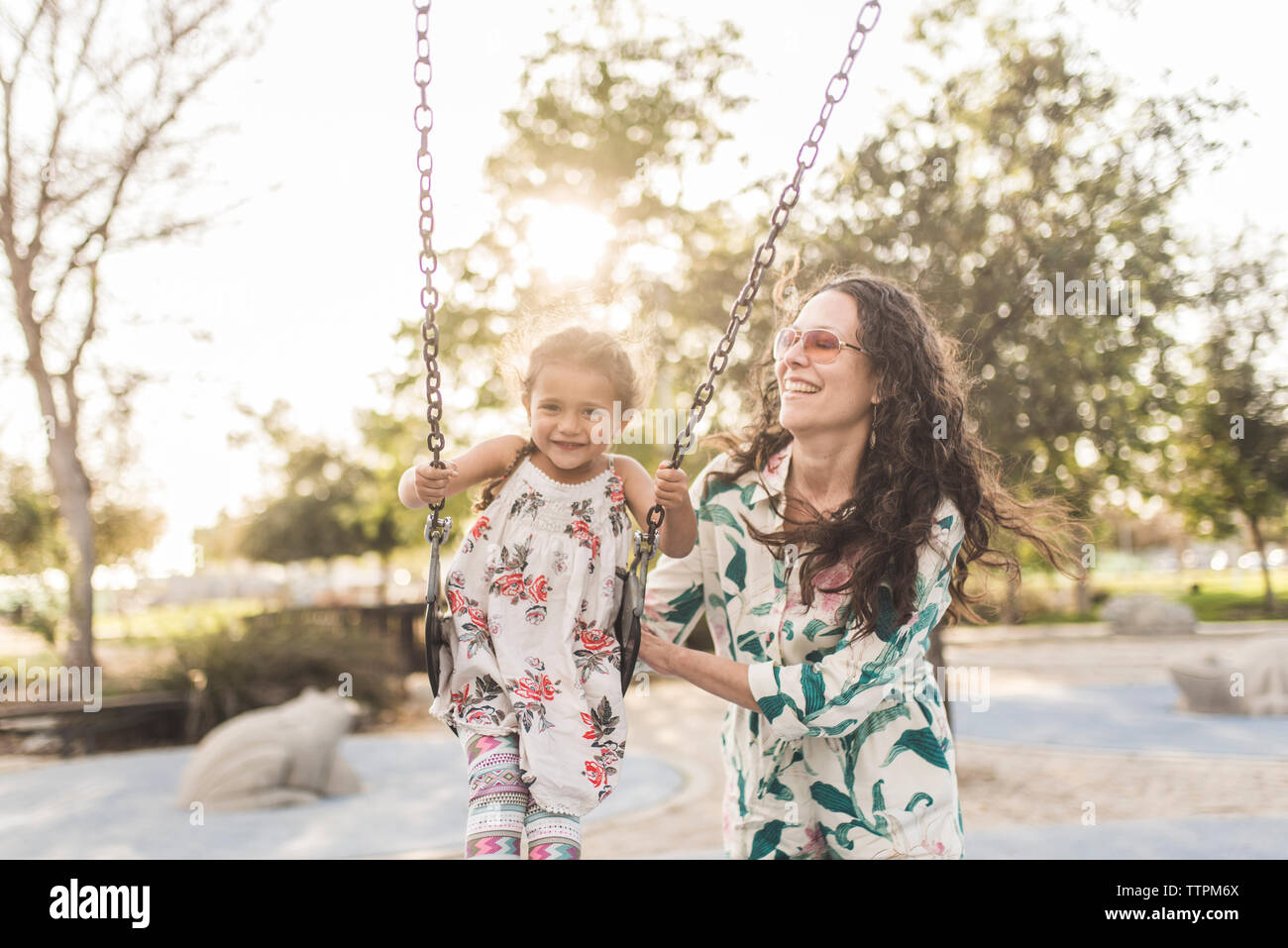 Happy mother pushing cute daughter swinging at playground Stock Photo - Alamy