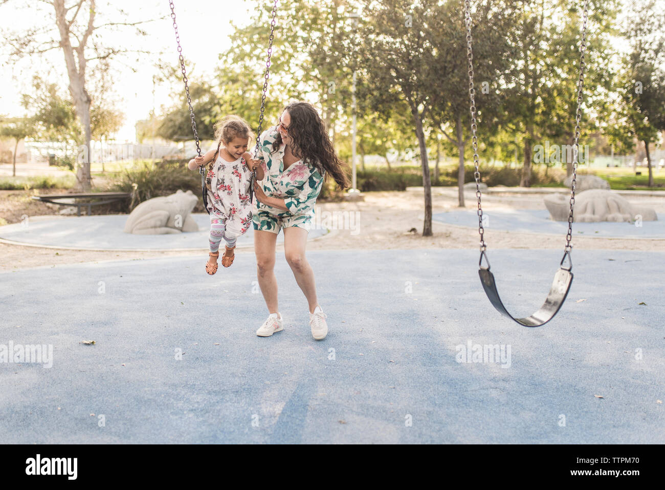Happy mother pushing daughter swinging at playground Stock Photo - Alamy