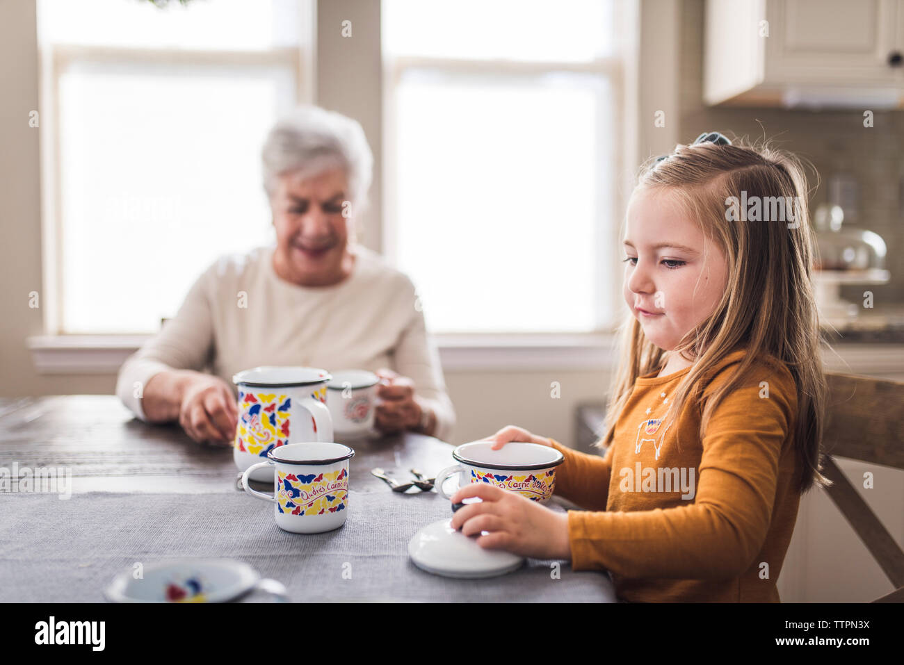 Granddaughter and great grandmother in kitchen playing with tea set ...