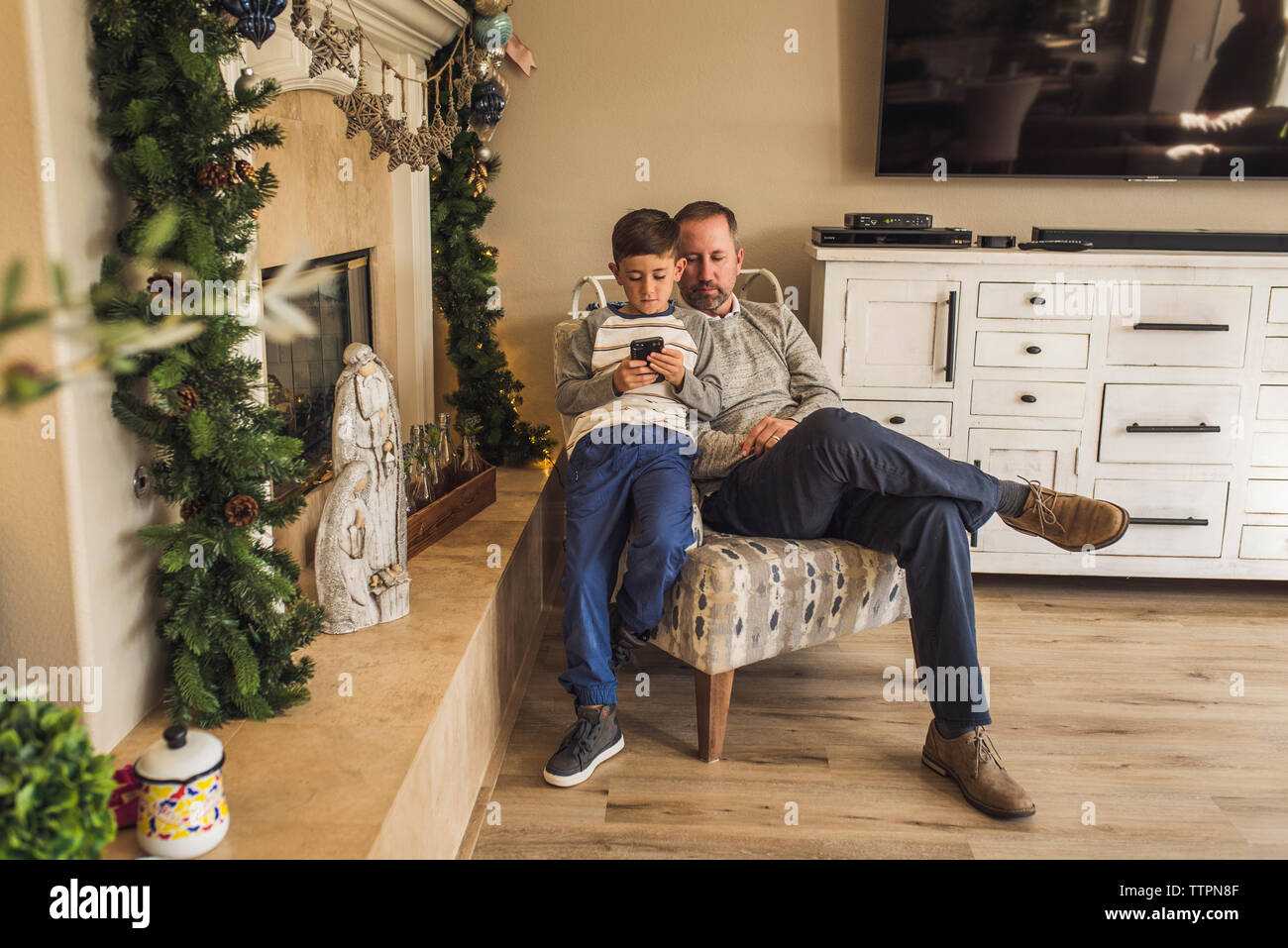 Elementary aged boy and father looking at phone in living room Stock ...