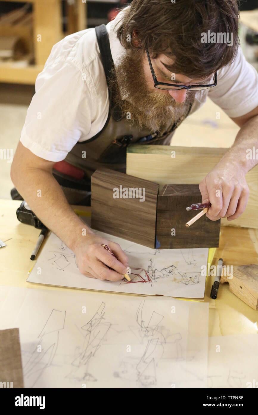 High angle view of carpenter drawing sketch while standing at workbench ...