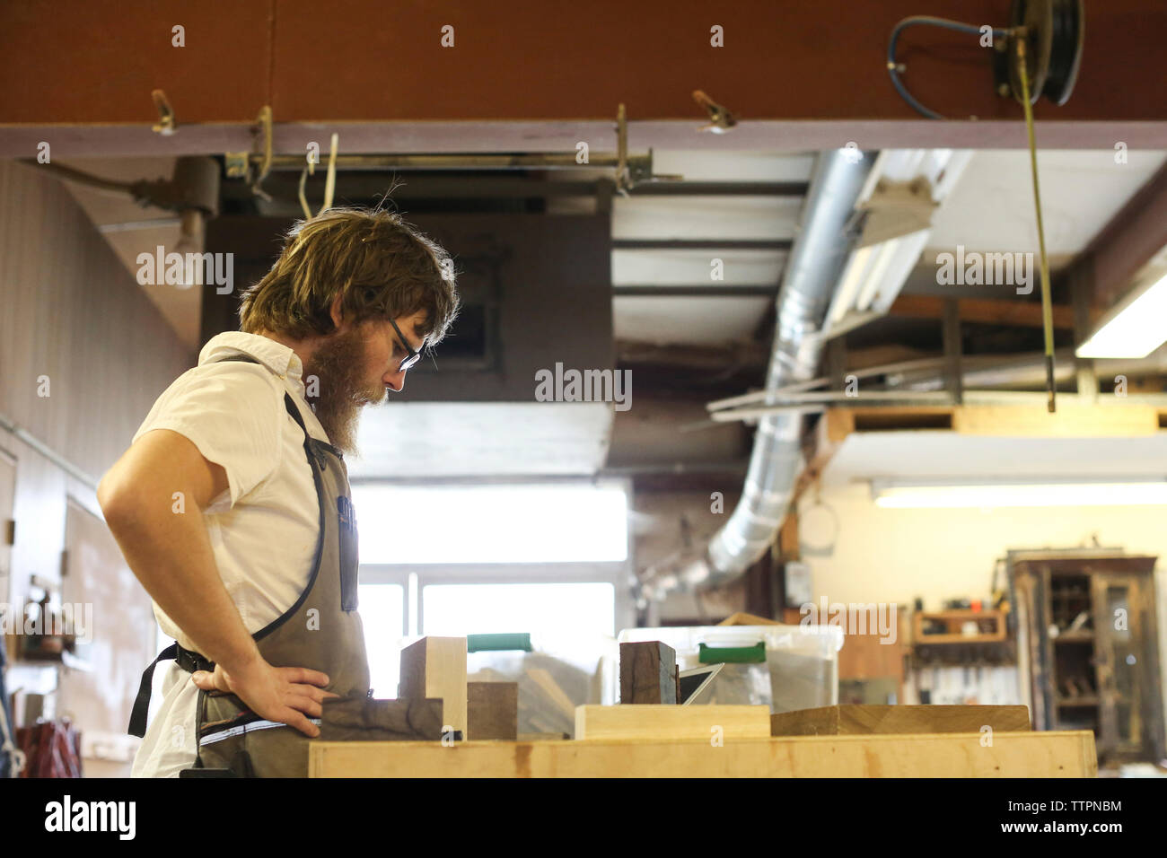 Side view of carpenter with hand on hip standing at workbench in ...