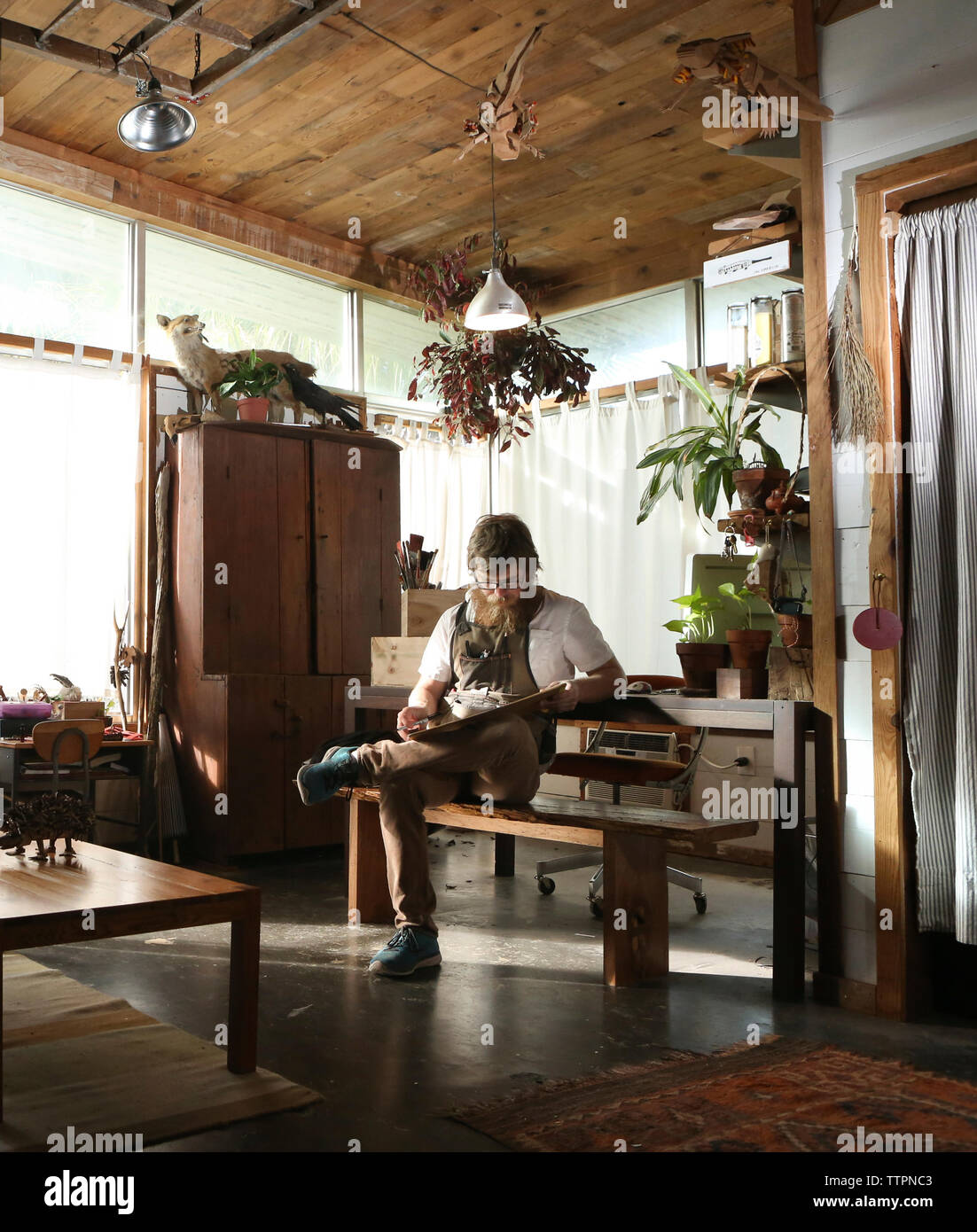 Full length of carpenter reading document while sitting on bench in ...