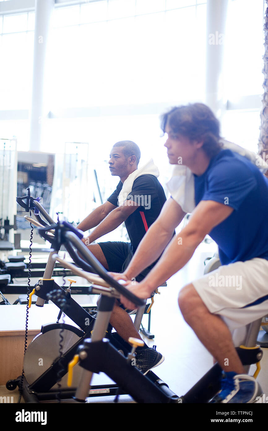 Side view of men riding exercise bikes in gym Stock Photo - Alamy