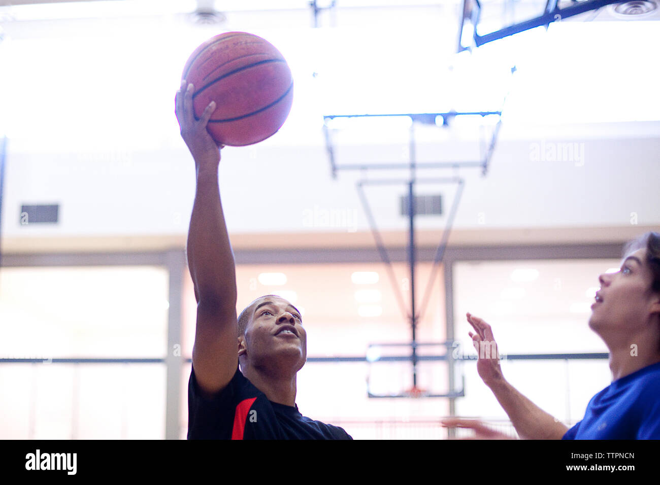 Basketball players playing in brightly lit court Stock Photo - Alamy