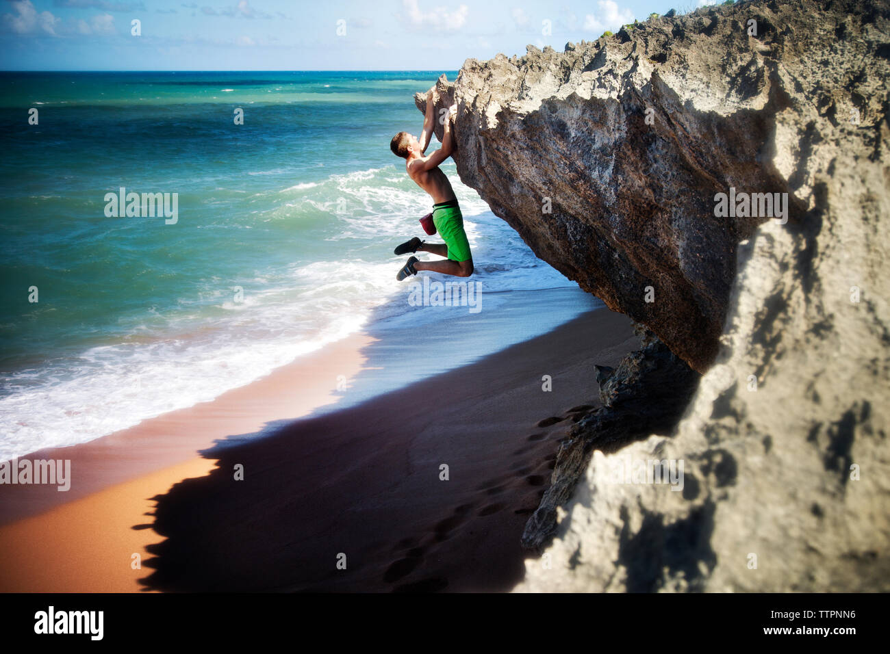 Side view of man rock climbing on beach Stock Photo - Alamy