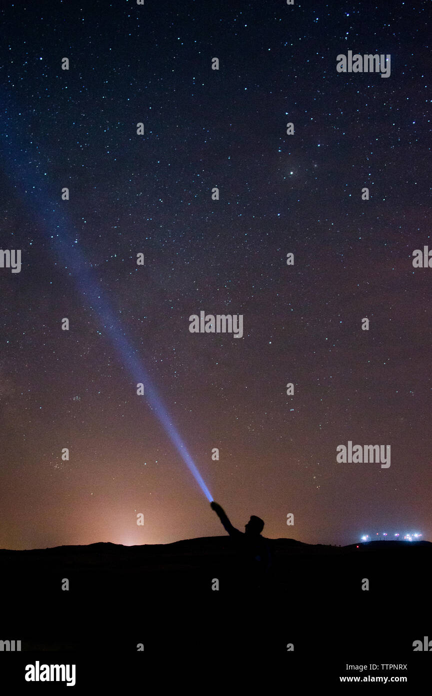 Silhouette man holding illuminated flashlight while standing against ...
