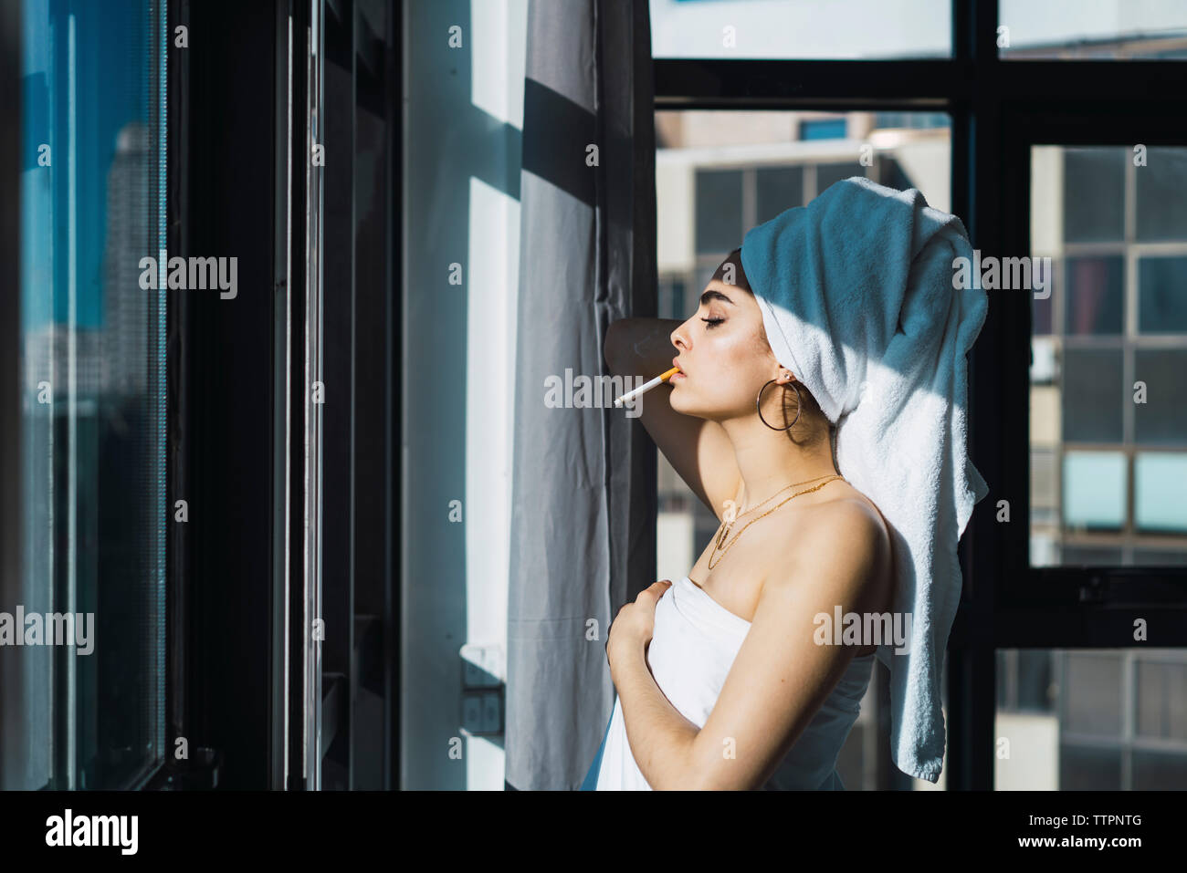 Young woman standing window smoking hi-res stock photography and images ...