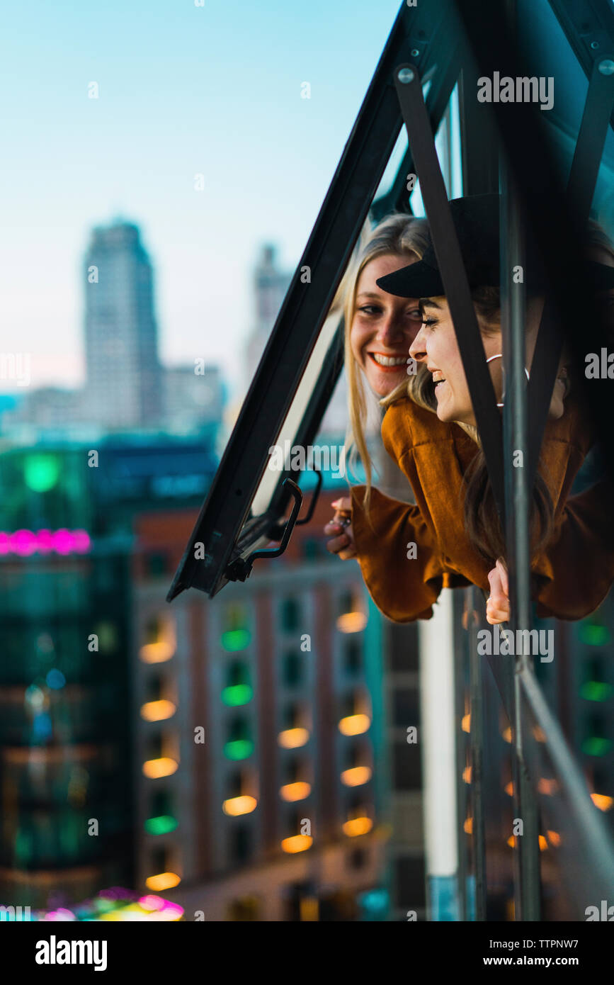 Happy female friends by building window Stock Photo - Alamy