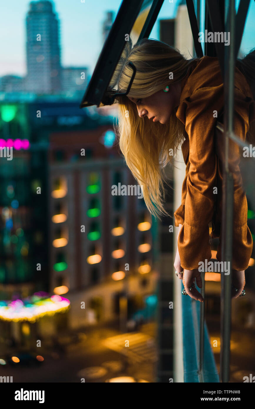 Side view of depressed young woman bending over window Stock Photo - Alamy