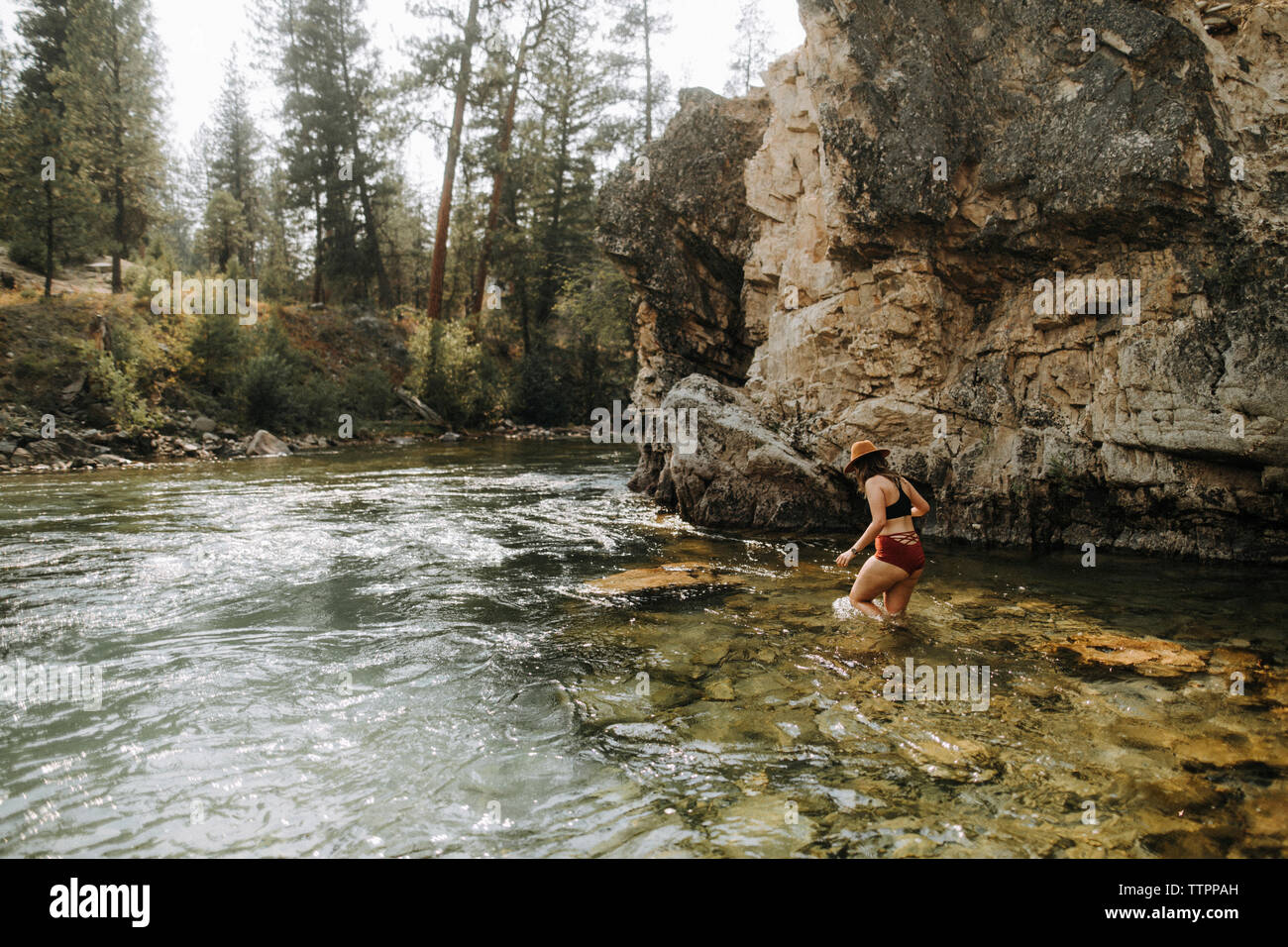 Side view of woman wearing bikini walking in river against rock ...